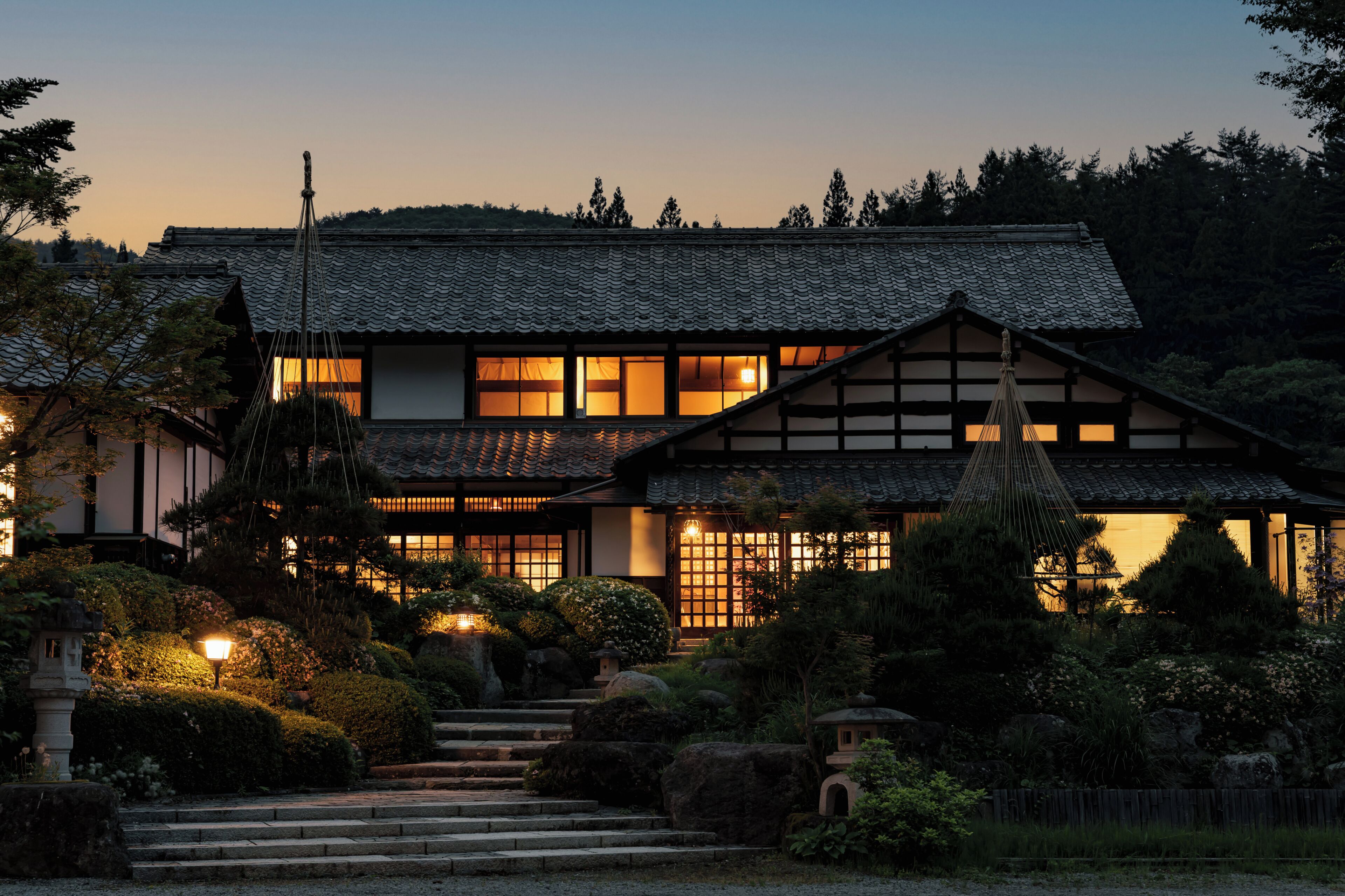 Uma casa tradicional japonesa com telhado telhado, vigas de madeira e um jardim bem cuidado, com degraus que levam à entrada.