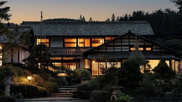 Uma casa tradicional japonesa com telhado telhado, vigas de madeira e um jardim bem cuidado, com degraus que levam à entrada.