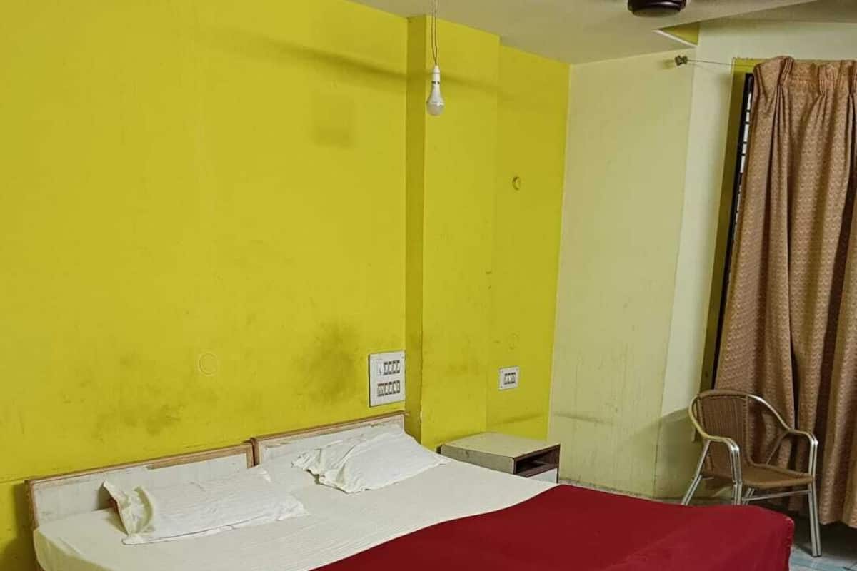 Uma cama de solteiro com um cobre-leito vermelho em um quarto com paredes amarelas e uma cortina marrom.