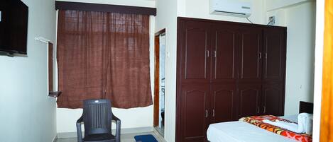 Quarto de hotel com cama, guarda-roupa, ar condicionado e uma secretária com cadeira.