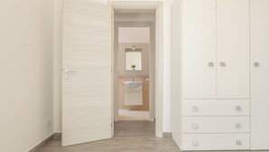 Quarto com porta de madeira, guarda-roupa branco e banheiro com pia e espelho.