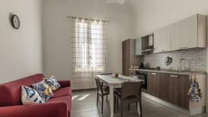 Um espaço compacto com cozinha compacta, área de refeições com mesa e cadeiras, e um sofá vermelho com almofadas estampadas.