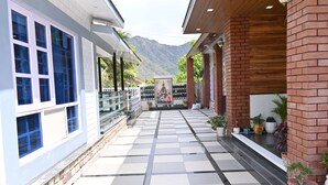 Um corredor com piso xadrez, plantas em vasos e vista para montanhas ao fundo.