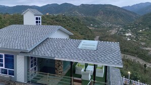 Um edifício moderno com telhado inclinado, janelas amplas e vista para um vale com montanhas.