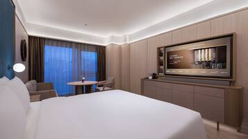 Quarto de hotel moderno com uma cama grande, uma mesa, uma cadeira, uma televisão e vista para a cidade pela janela.