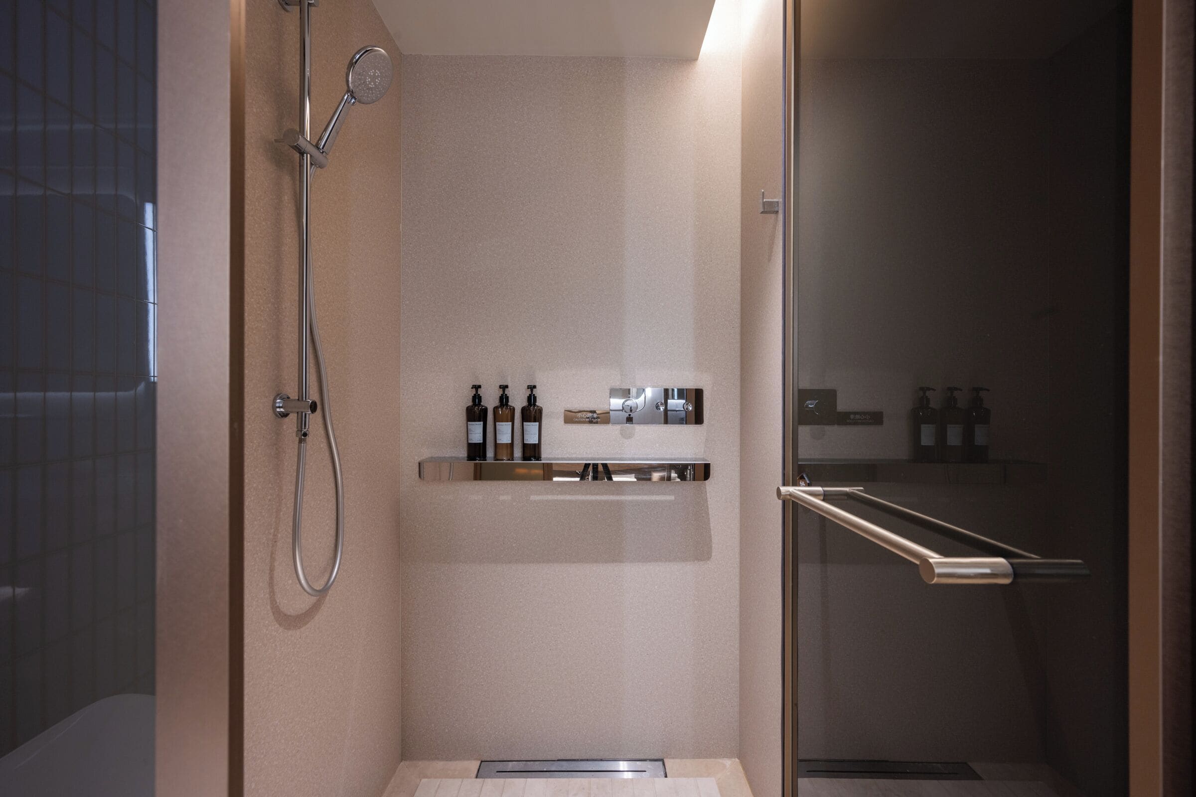 Casa de banho moderna com chuveiro, porta de vidro, lavatório com espelho e prateleira com produtos de higiene pessoal.