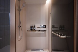 Casa de banho moderna com chuveiro, porta de vidro, lavatório com espelho e prateleira com produtos de higiene pessoal.
