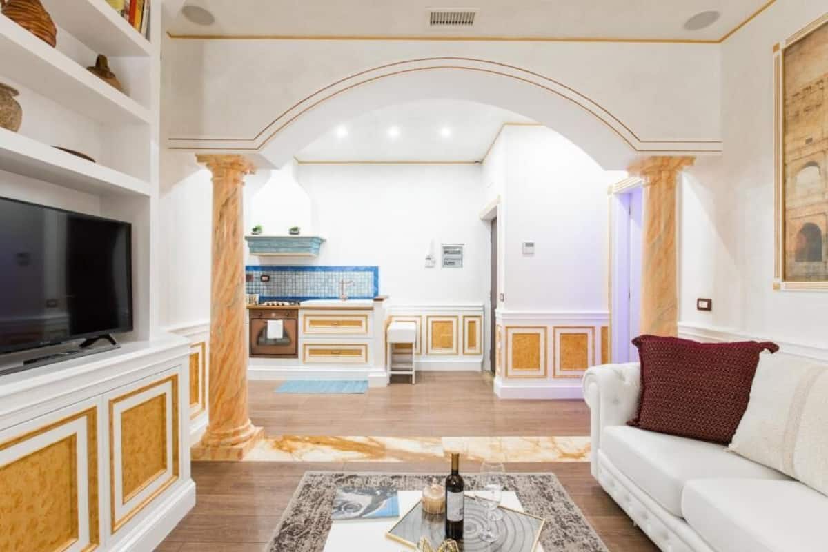 Uma sala de estar ampla com televisão, uma mesa de centro de mármore e um sofá branco.