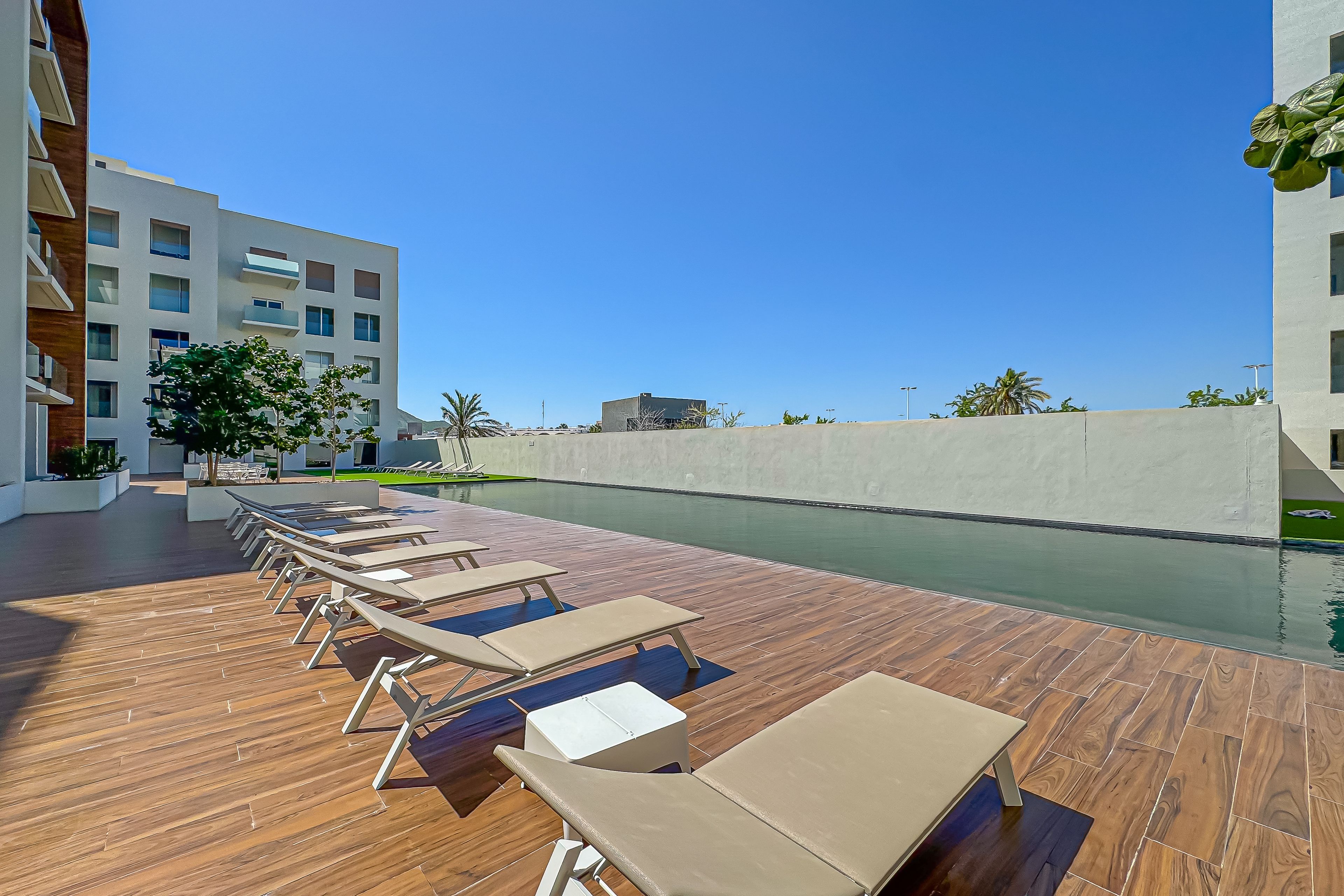 Uma área à beira da piscina com espreguiçadeiras e um edifício moderno ao fundo.