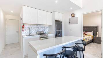Uma cozinha moderna com armários brancos, bancada de mármore e uma ilha central com banquetas.