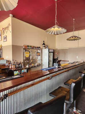 Uma área de bar com balcão, assentos e geladeira abastecida com bebidas.