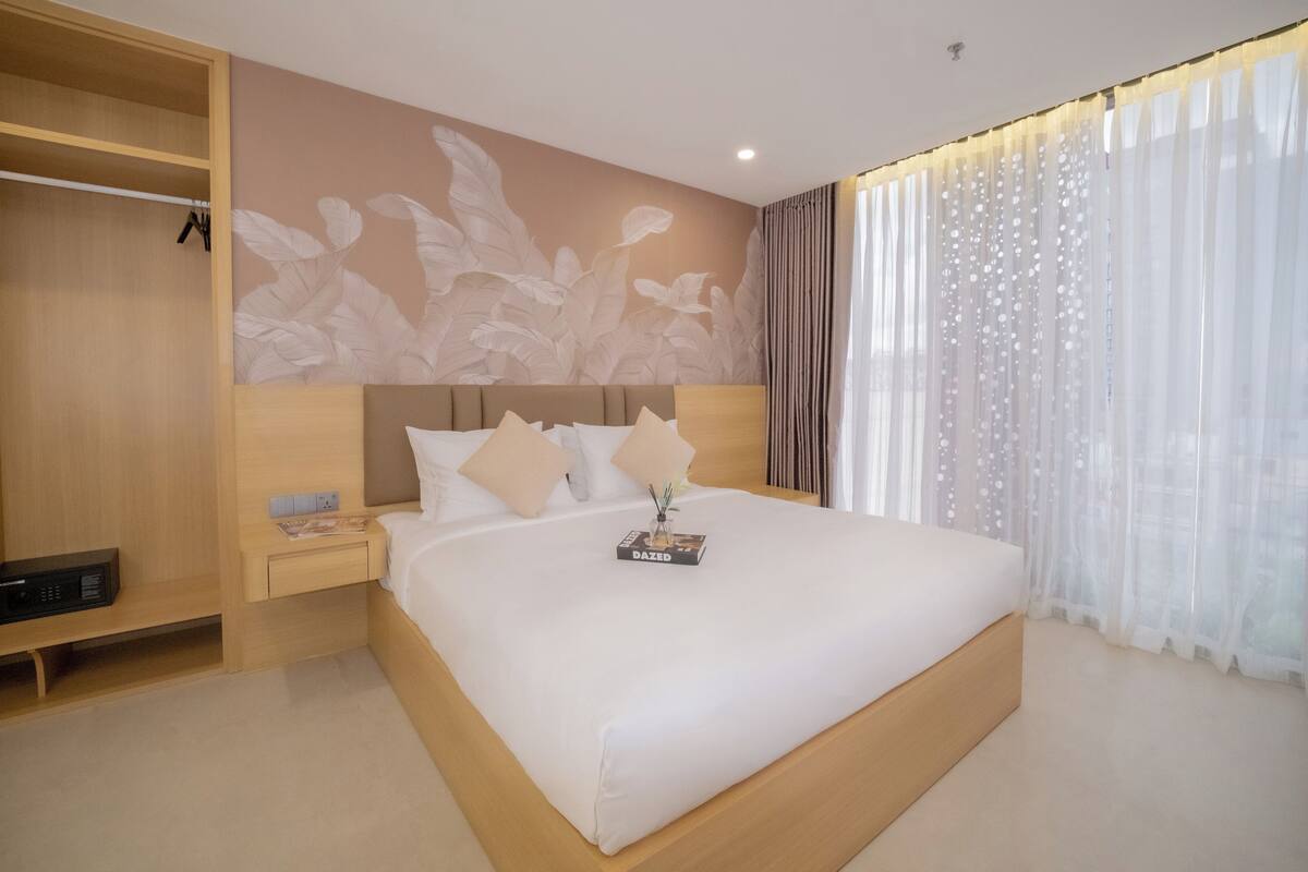 Quarto de hotel com uma cama grande, um guarda-roupa de madeira, uma mesa de cabeceira e uma parede com um mural floral.