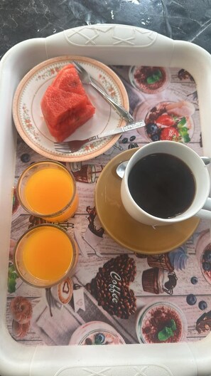 Uma bandeja com uma fatia de melancia, dois copos de suco de laranja e uma xícara de café preto.