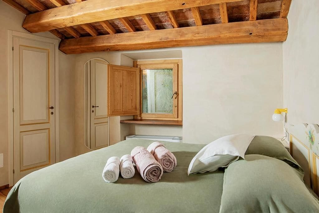 Quarto com cama, toalhas dobradas, janela, vigas de madeira e porta.