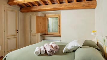 Quarto com cama, toalhas dobradas, janela, vigas de madeira e porta.