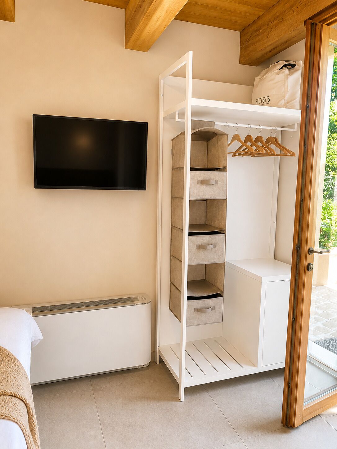 Um quarto com um guarda-roupa branco, uma televisão fixada na parede e um radiador.