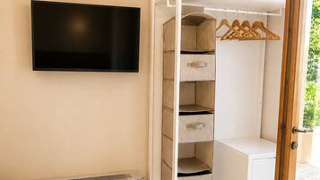 Um quarto com um guarda-roupa branco, uma televisão fixada na parede e um radiador.