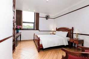 Quarto com cama de madeira, mesas de cabeceira, um criado-mudo, janela com cortinas e um ventilador.