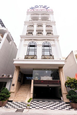 Entrada de hotel com chão xadrez, escadaria e placa indicando 'The Eastern Hotel & Apartment'.