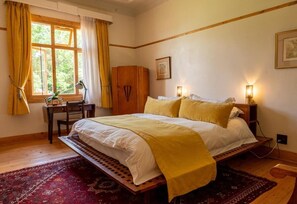 Quarto com cama de madeira, escrivaninha, guarda-roupa e janela com cortinas.