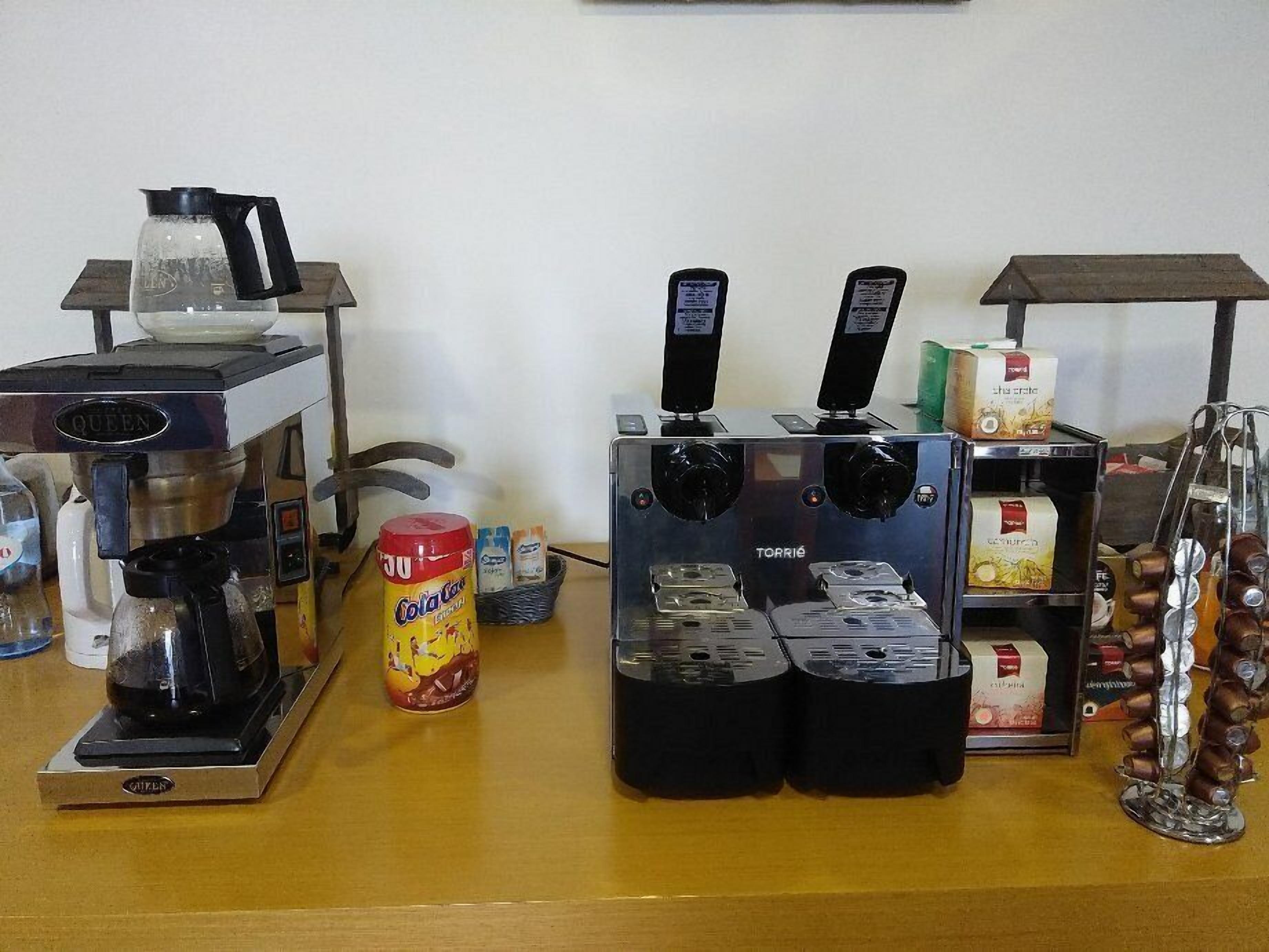Uma máquina de café, um pote de Colasa e uma prateleira com cápsulas de café.