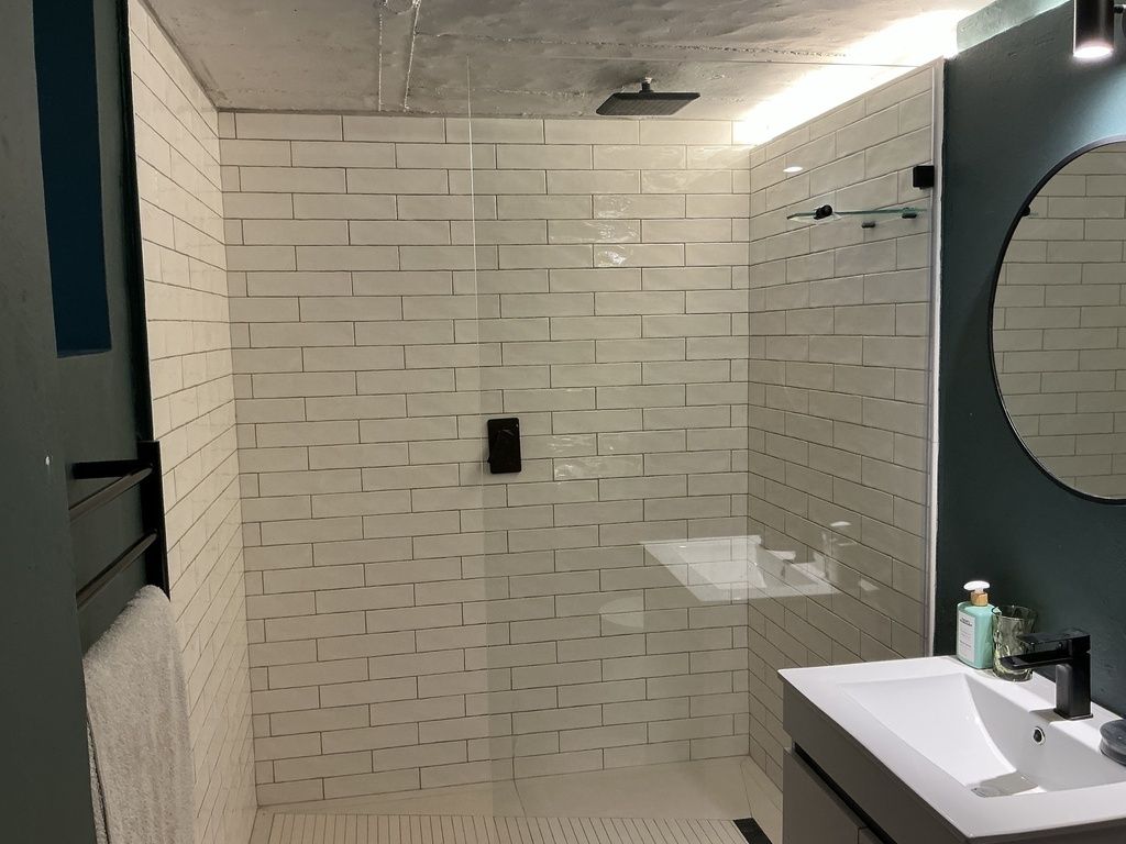 Casa de banho moderna com azulejos brancos tipo metrô, cabine de chuveiro em vidro, lavatório branco e espelho redondo.