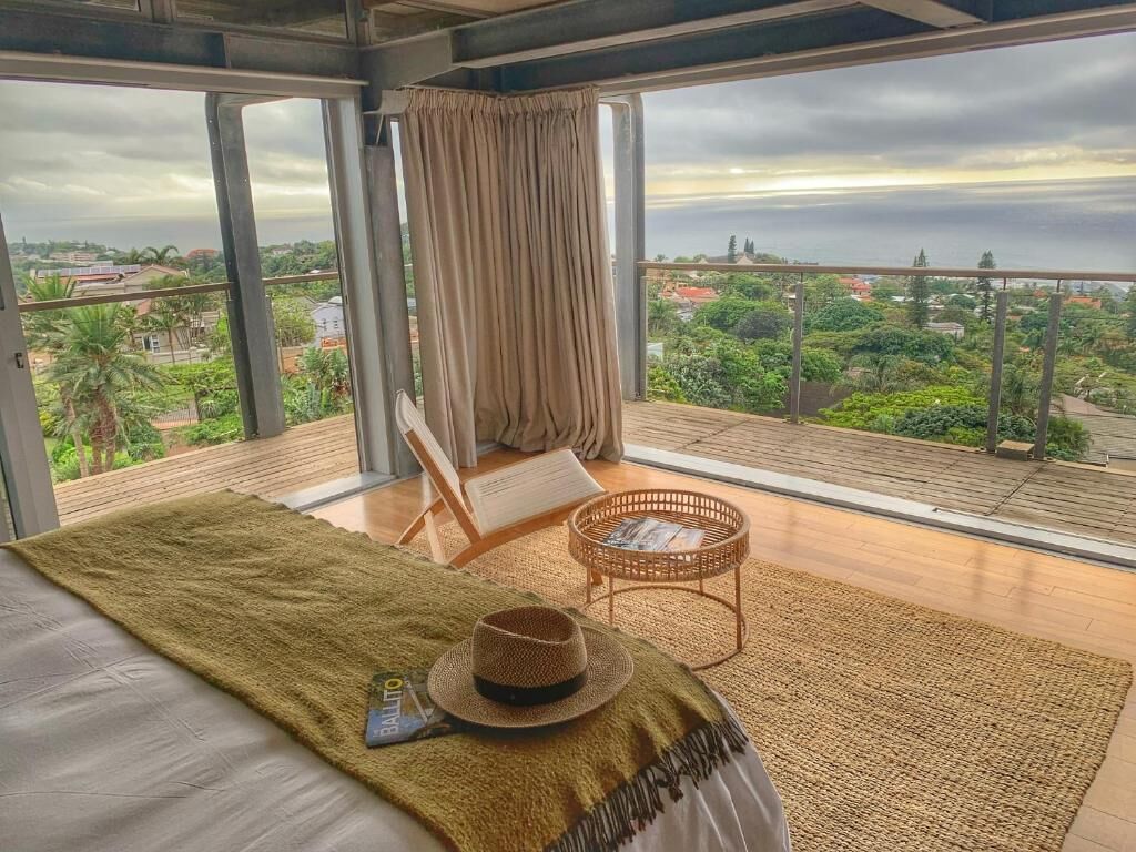 Quarto com uma cama grande, janela com cortinas, cadeira de vime e uma mesinha de centro com revistas.