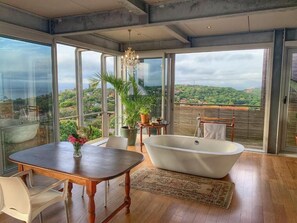 Um banheiro moderno com uma banheira independente, uma mesa de madeira com cadeiras e uma janela grande com vista para uma paisagem montanhosa.