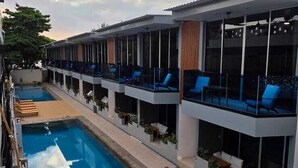 Um hotel moderno com piscina, área de estar ao ar livre e um espaço coberto com cadeiras azuis.