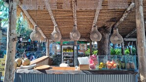 Um charmoso bar ao ar livre para café e sucos, com telhado de palha, luminárias pendentes e uma variedade de frutas e bebidas frescas.