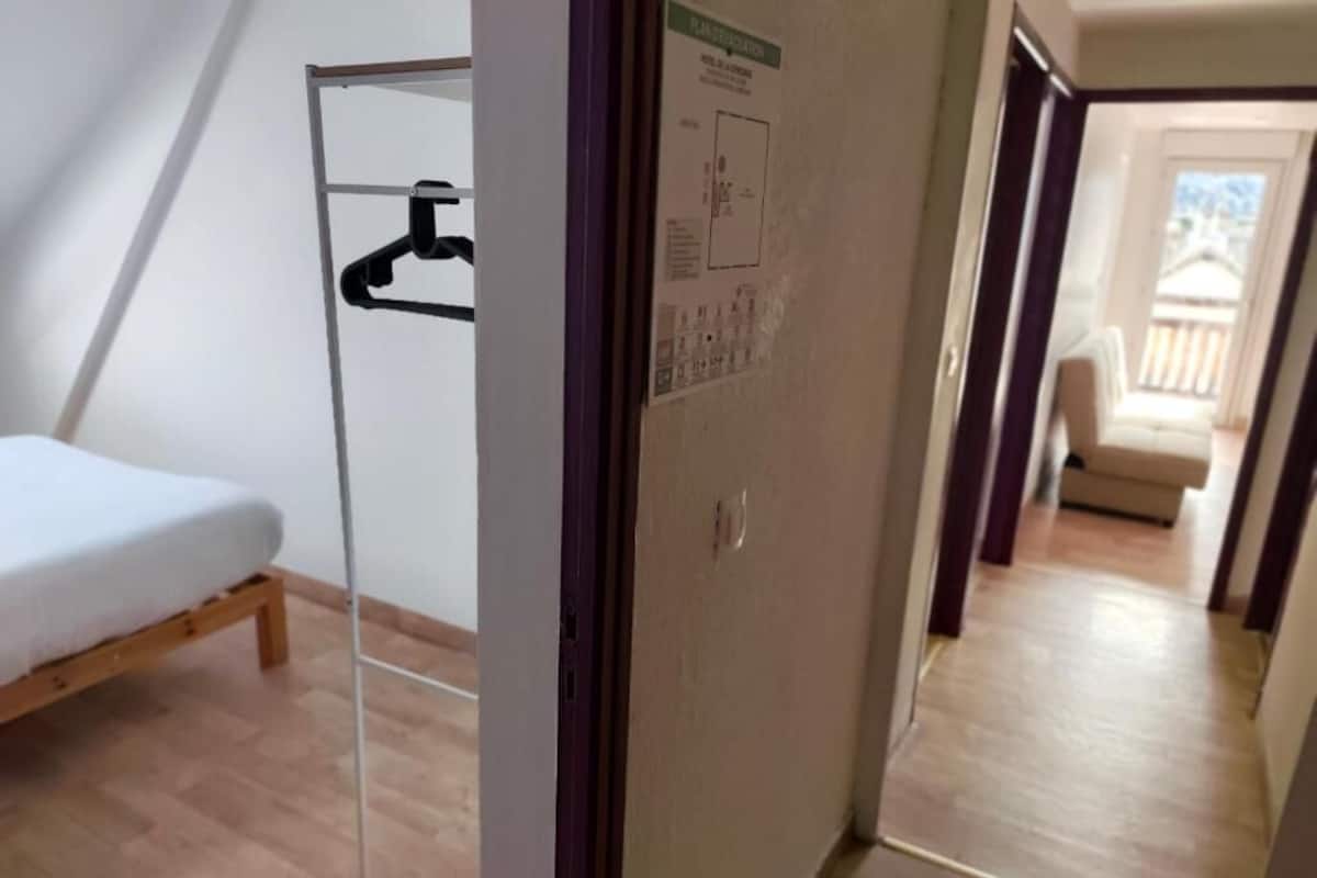 Quarto com cama, cabideiro e porta com placa de identificação do plano.