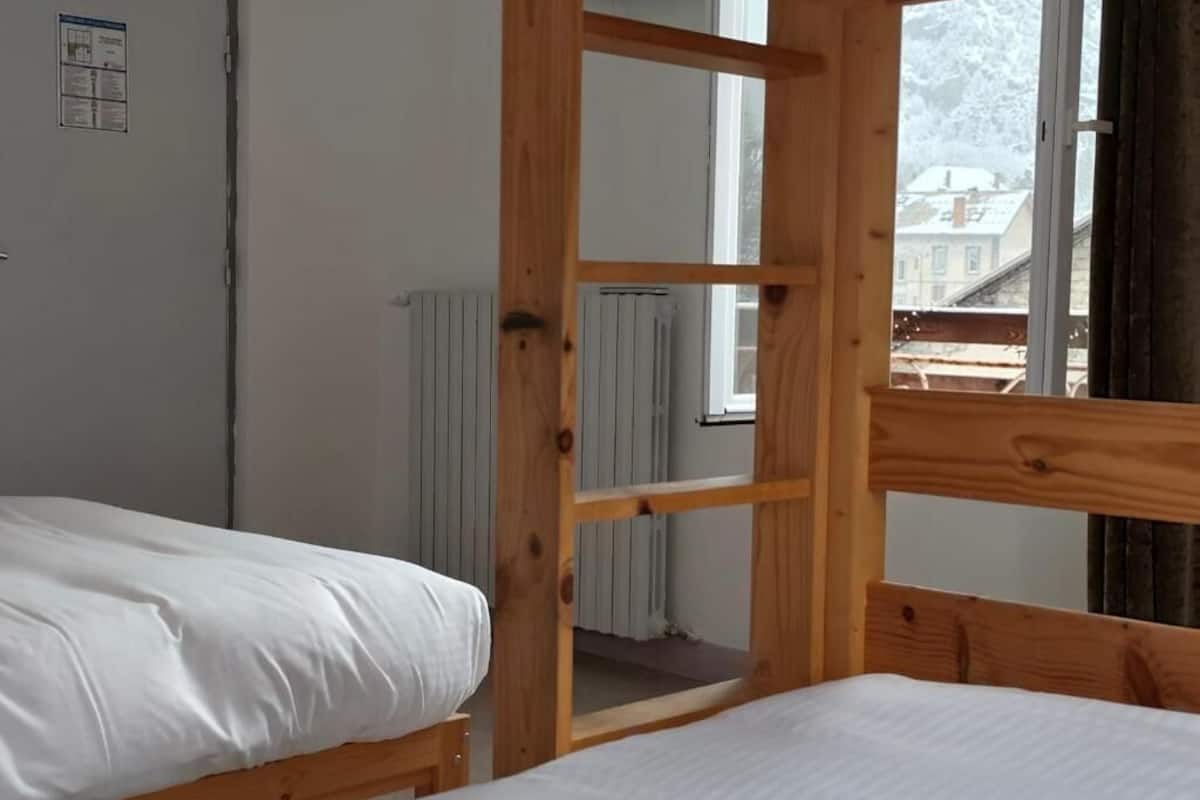 Um quarto com uma cama de madeira beliche, janela com vista para edifícios e um radiador na parede.