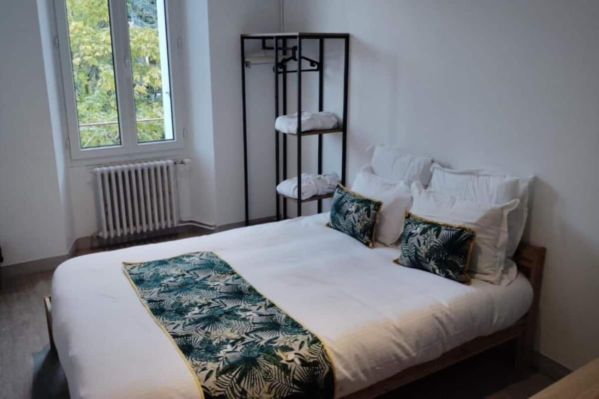 Quarto com cama, radiador, janela e cabideiro.