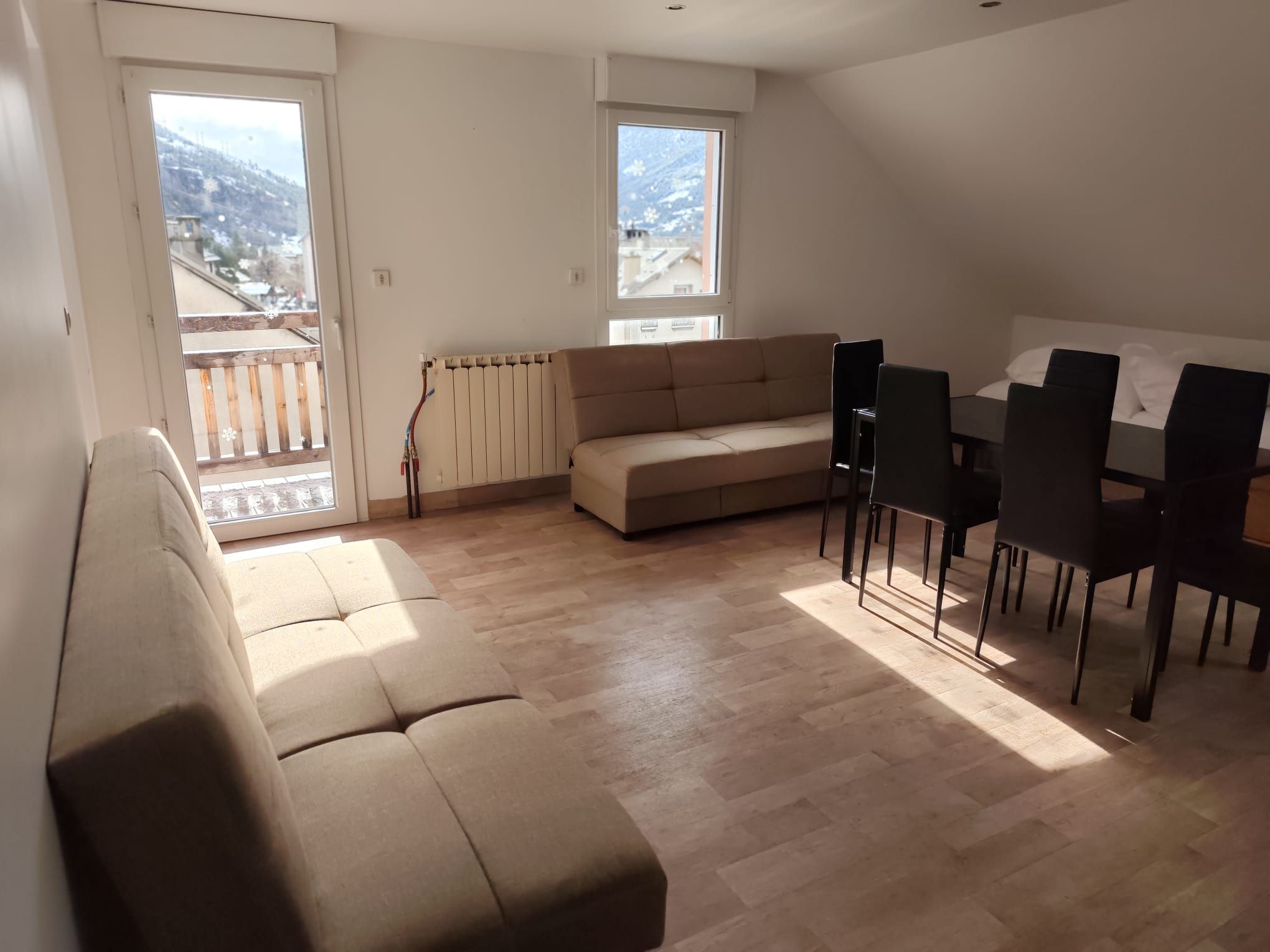 Quarto com sofá, mesa de jantar e cadeiras, e vista pela janela.
