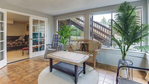 Quarto com uma mesa de jantar, móveis de vime, uma planta em vaso e vista para um edifício.