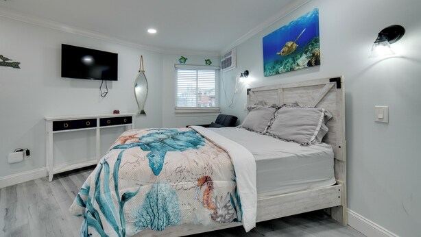 Quarto com cama, televisão, janela com persianas e luminária.