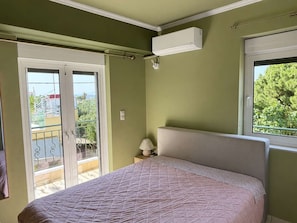 Quarto com cama, janela, porta de varanda e ar condicionado.