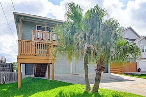 Uma casa de dois andares com varanda, garagem e um gramado com palmeiras.
