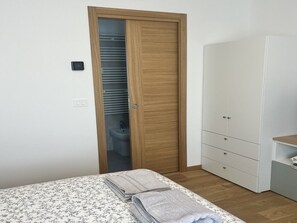 Quarto com guarda-roupa de madeira, cama com colcha florida e um armário branco.