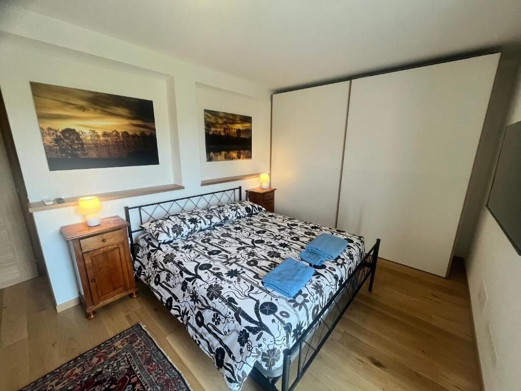 Quarto com cama, mesas de cabeceira, tapete e duas pinturas penduradas na parede.