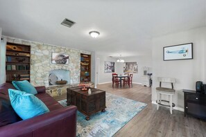 Uma sala de estar com lareira de pedra, sofá de couro vermelho, mesa de centro e área de jantar com cadeiras.