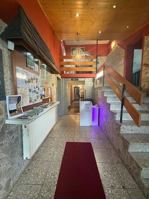 Um saguão de hotel com balcão de recepção, escadaria e um candelabro.