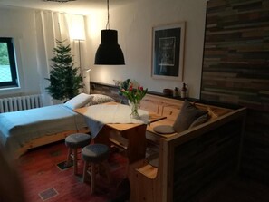 Um quarto acolhedor com uma cama, uma mesa de jantar com banquetas, um pequeno pinheiro de Natal e um candeeiro suspenso.