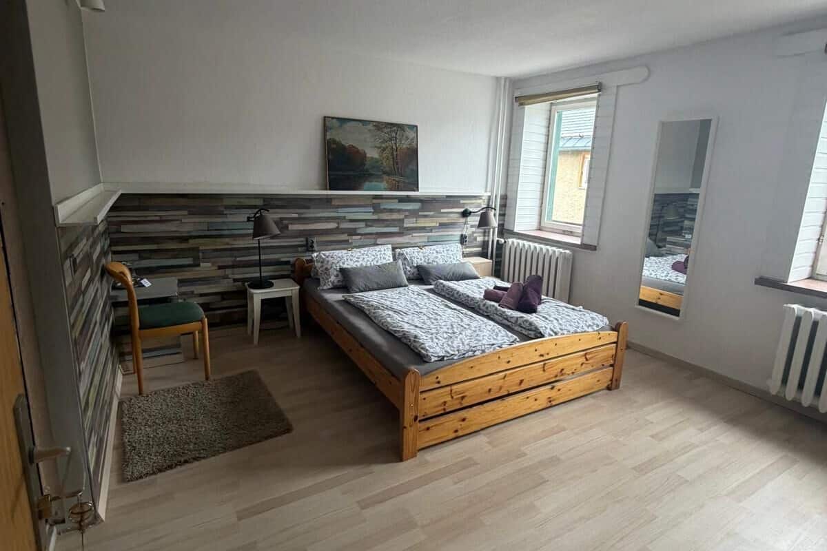 Quarto com cama de madeira, quadro na parede, janela e radiador.