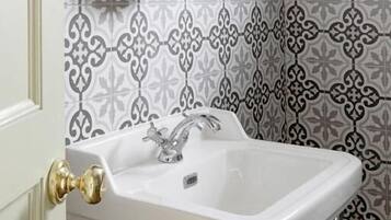 Casa de banho com lavatório branco, espelho e papel de parede estampado.