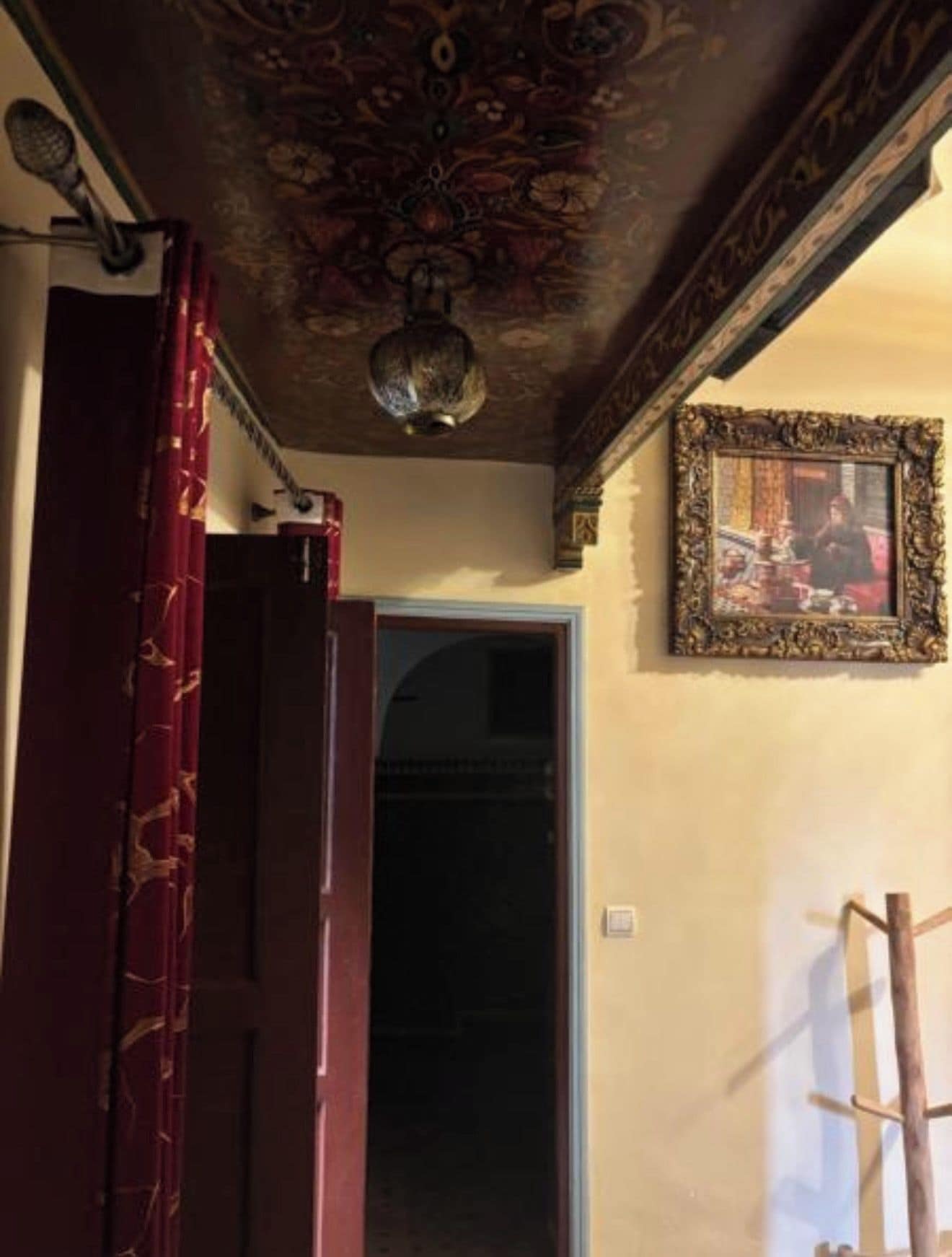 Um quarto com teto estampado, uma moldura na parede e uma escada de madeira encostada.