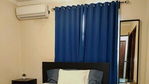 Quarto com cama, mesa de cabeceira, ar condicionado, espelho e cortinas azuis.