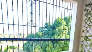 Varanda com mesa redonda e quatro cadeiras, um vaso de planta e vista para o verde.