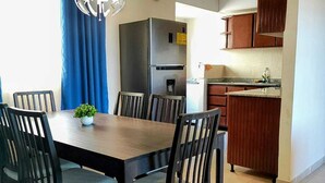Uma sala de jantar com mesa e cadeiras de madeira, geladeira moderna e cozinha com armários de madeira.
