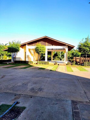 Um edifício com varanda coberta, céu claro e gramado bem cuidado.